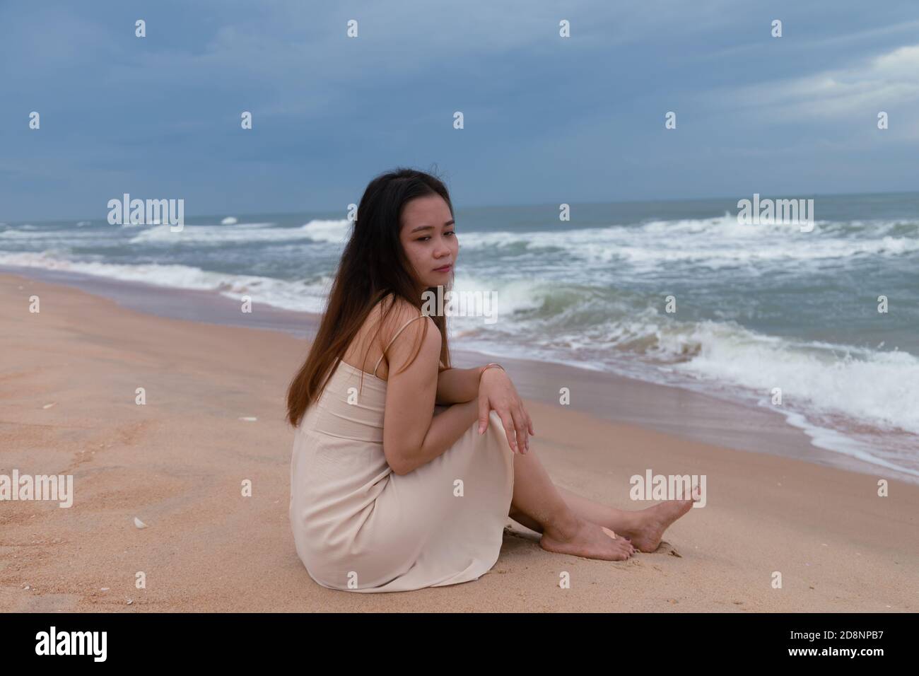Beautiful Asian woman sitting on the sand near the beach and enjoying ...