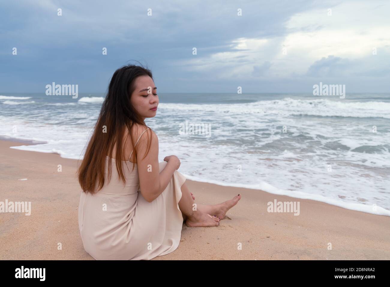 Beautiful Asian woman sitting on the sand near the beach and enjoying ...