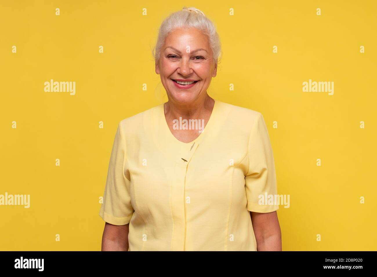 Senior woman smiling happily laughing at the camera on yellow wall ...