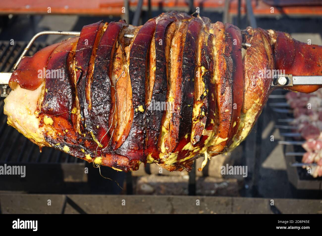 A crispy piece of pork on a rotisserie spit at a barbecue event. large ...