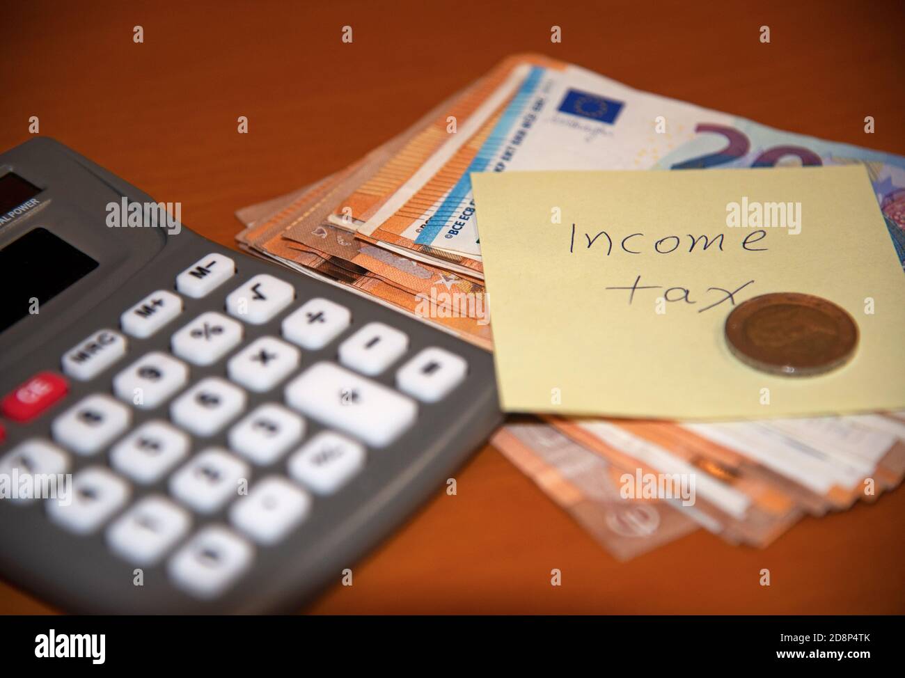 Income tax written on post-it note with bank notes, a coin and a ...