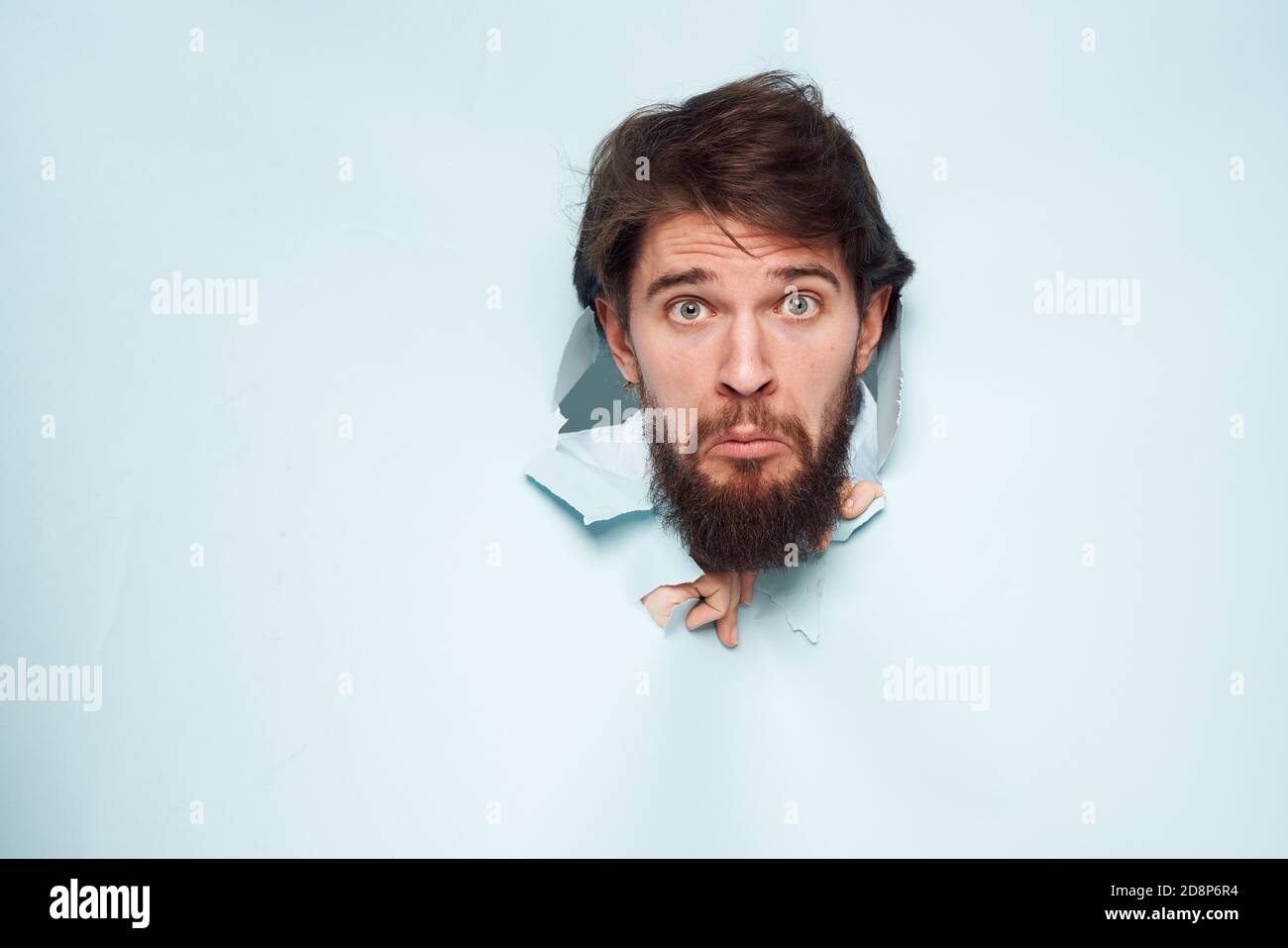 Closeup of a young man peeking from behind books on shelf in library ...