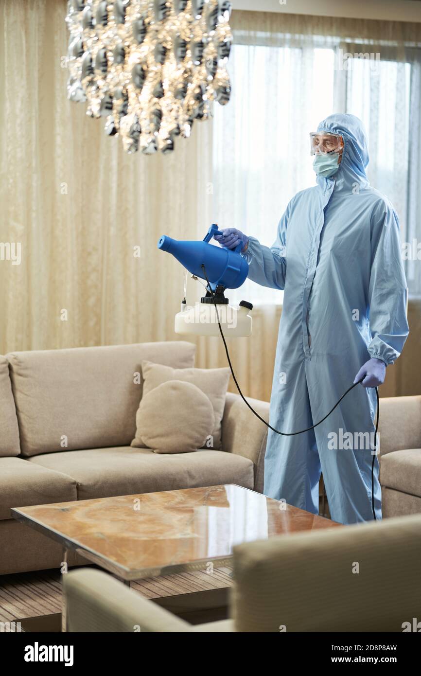 Worker in blue chemical protection suit doing disinfection and spraying ...