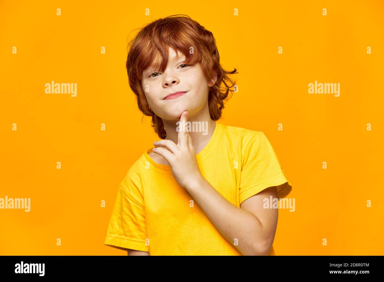 smiling red-haired child on a yellow background holds his hand near the ...