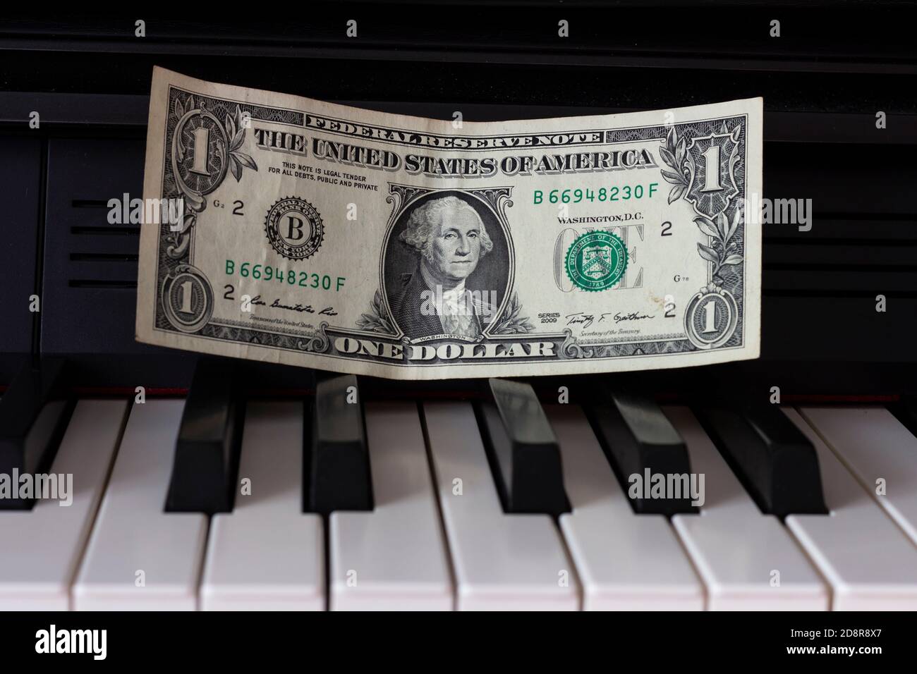 One dollar banknote lying on the piano keys. The dollar as a symbol of ...