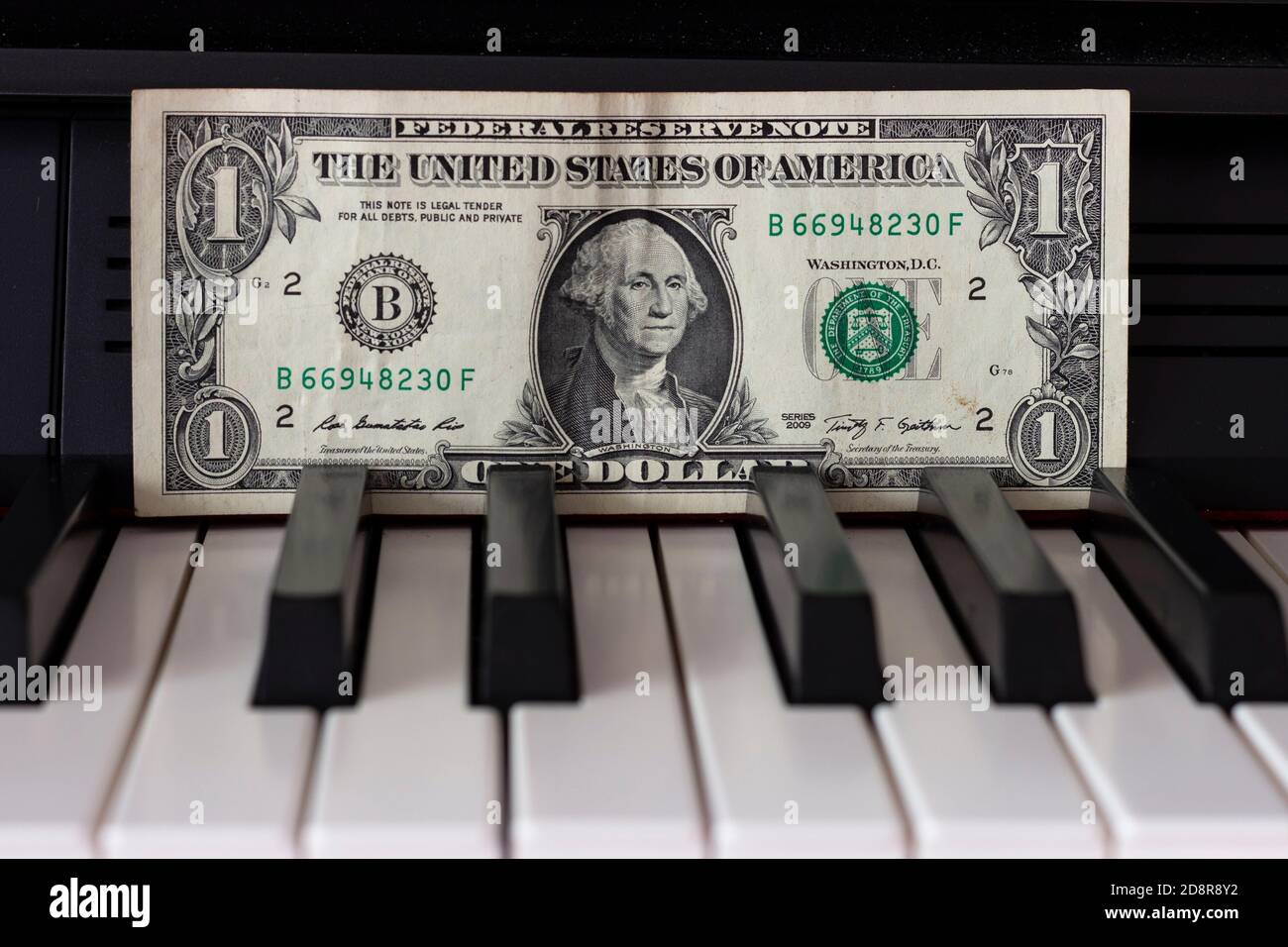One dollar banknote lying on the piano keys. The dollar as a symbol of ...