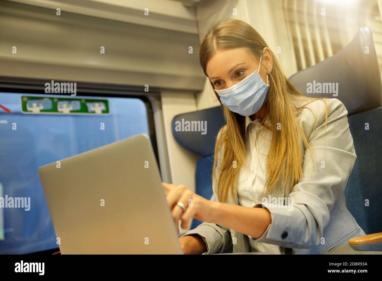 Businesswoman commuting by train, working on laptop and wearing face ...