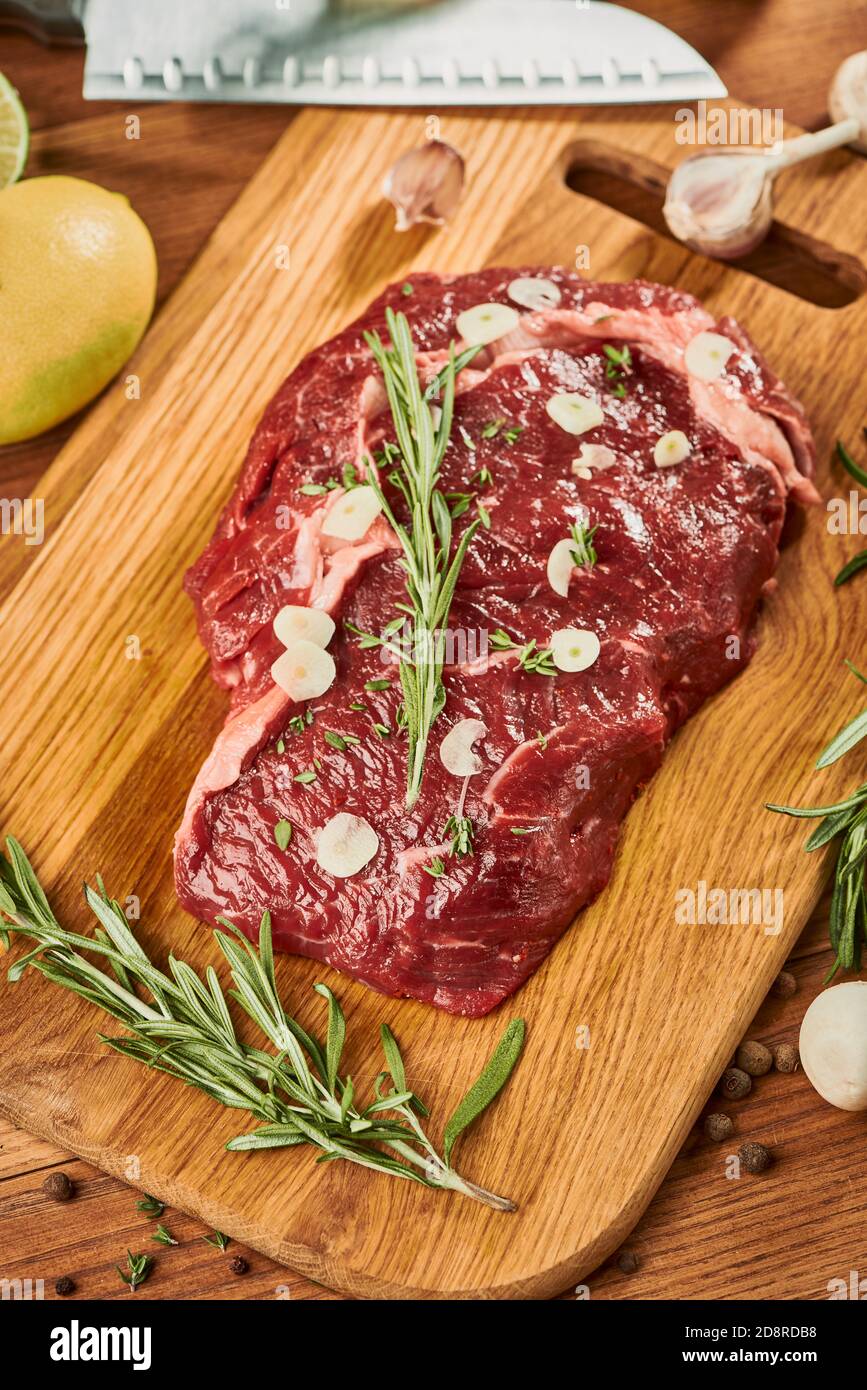 Top view on a raw meat being seasoned with fresh thyme, rosemary and ...
