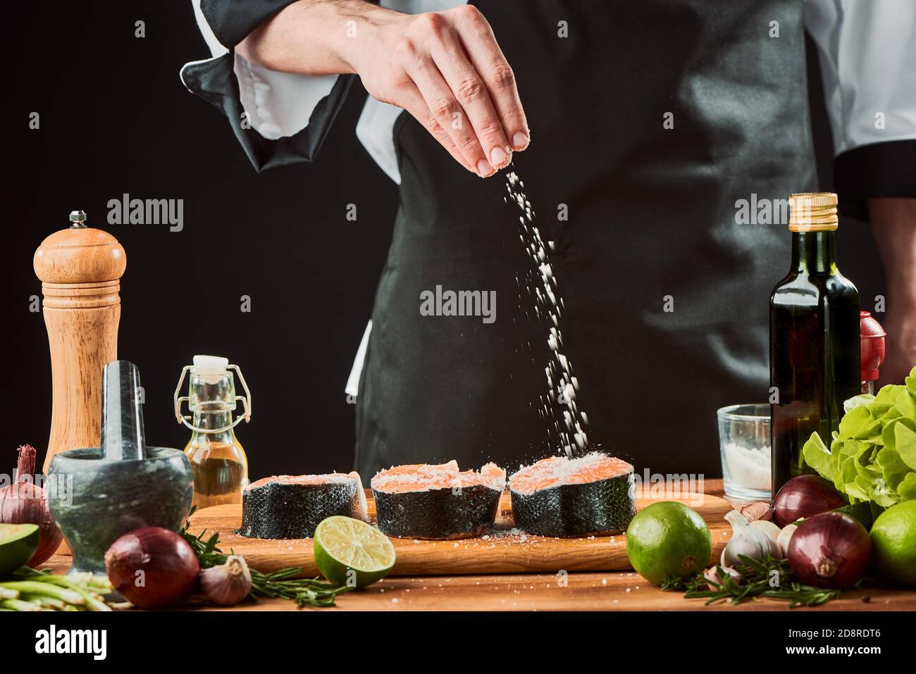 Chef sprinkles salt onto fish. Professional cook seasoning salmon ...