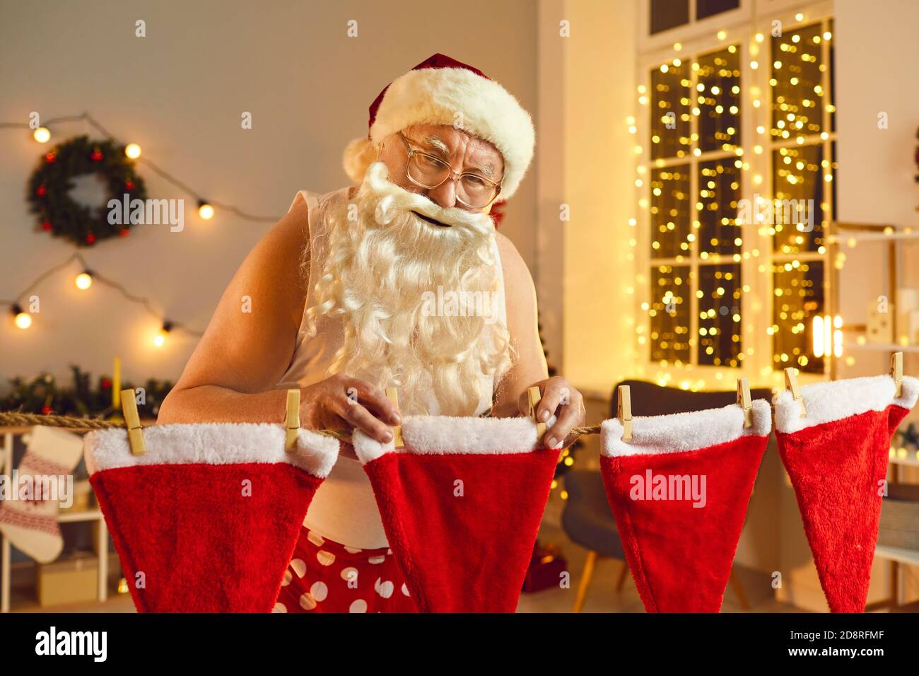 Cute senior Santa Claus hangs to dry his Christmas hats on a string ...