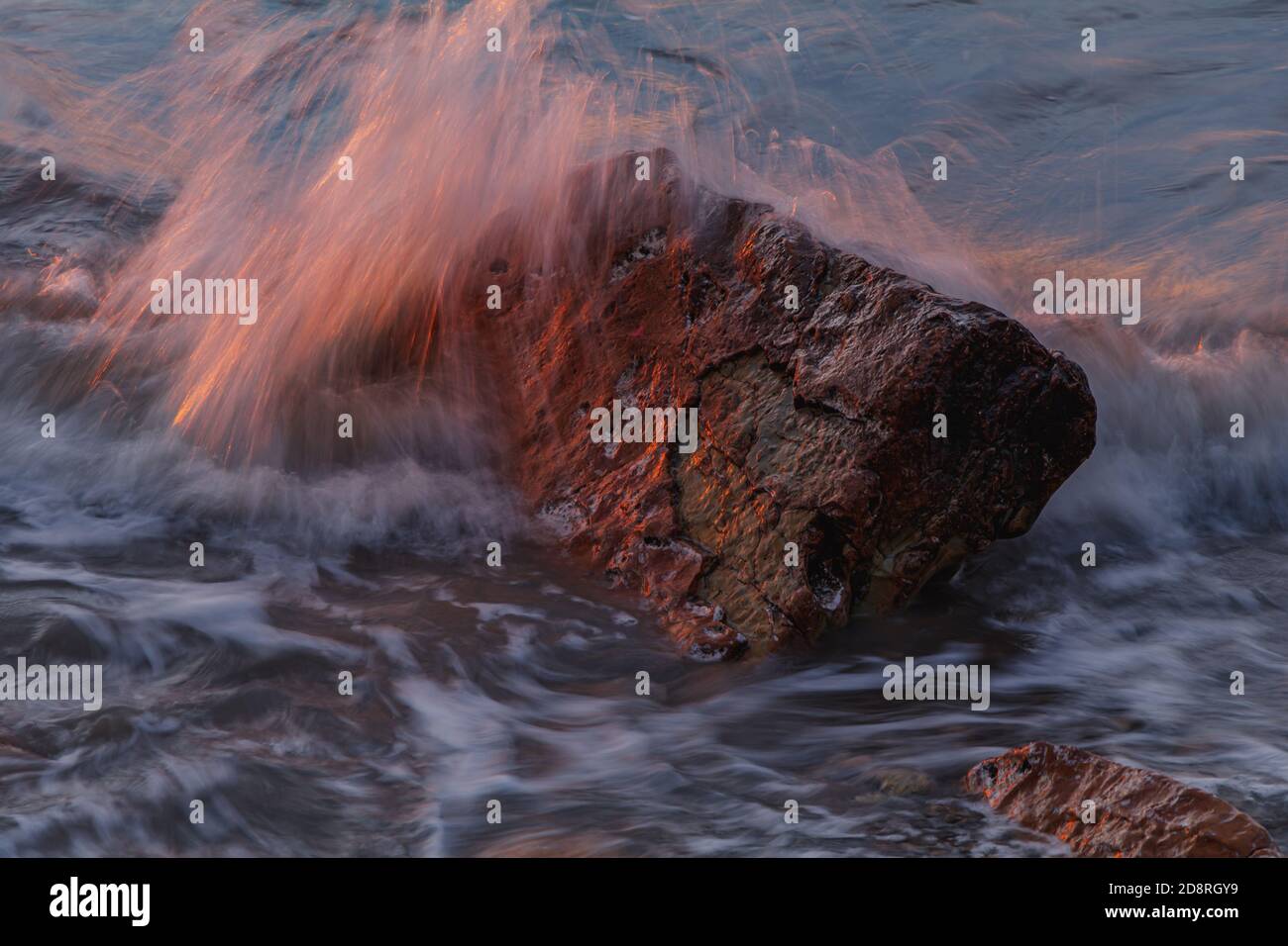 The rock catching the last of the sunlight with small wave breaking ...