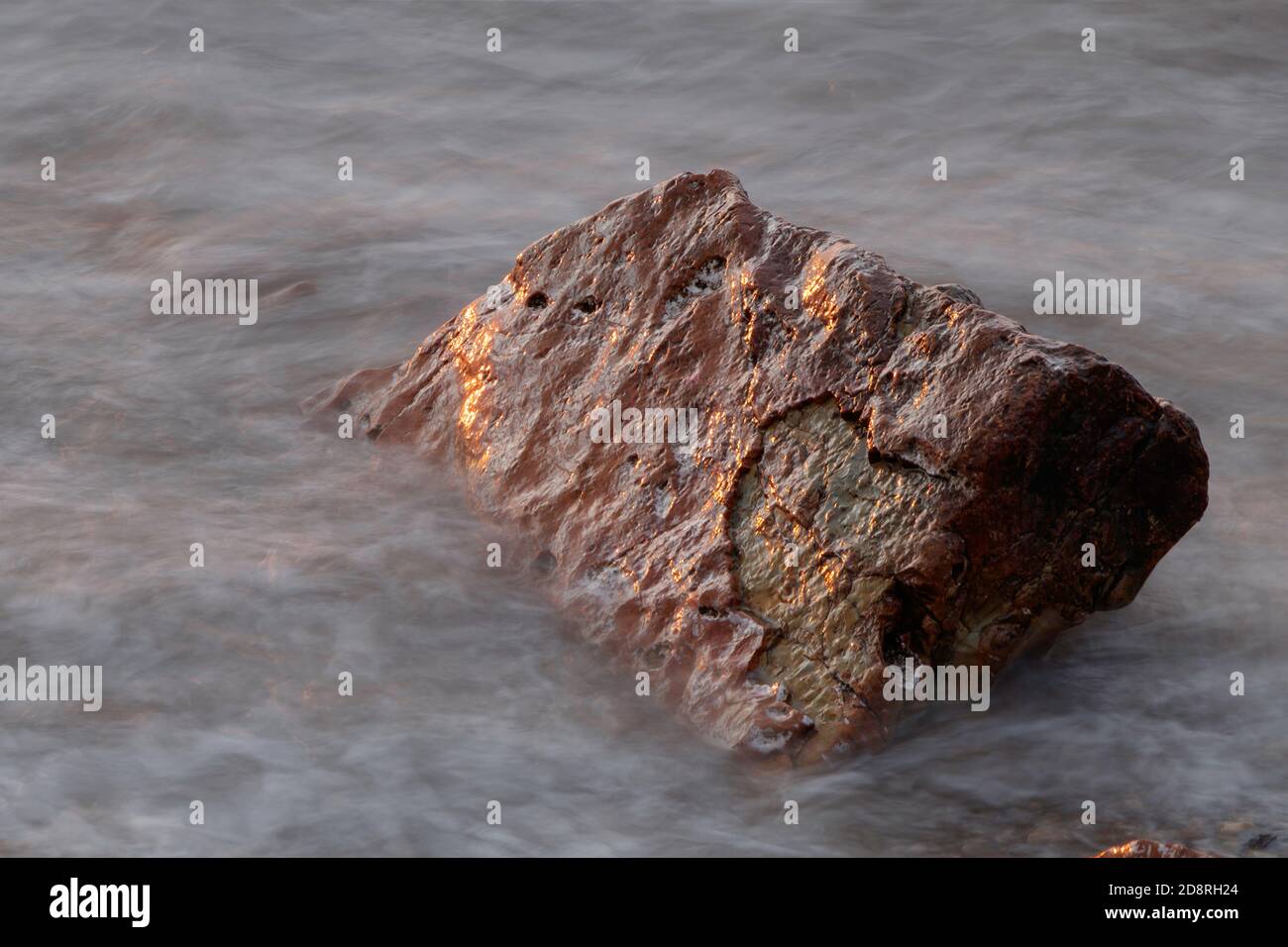 The rock catching the last of the sunlight with small wave breaking ...