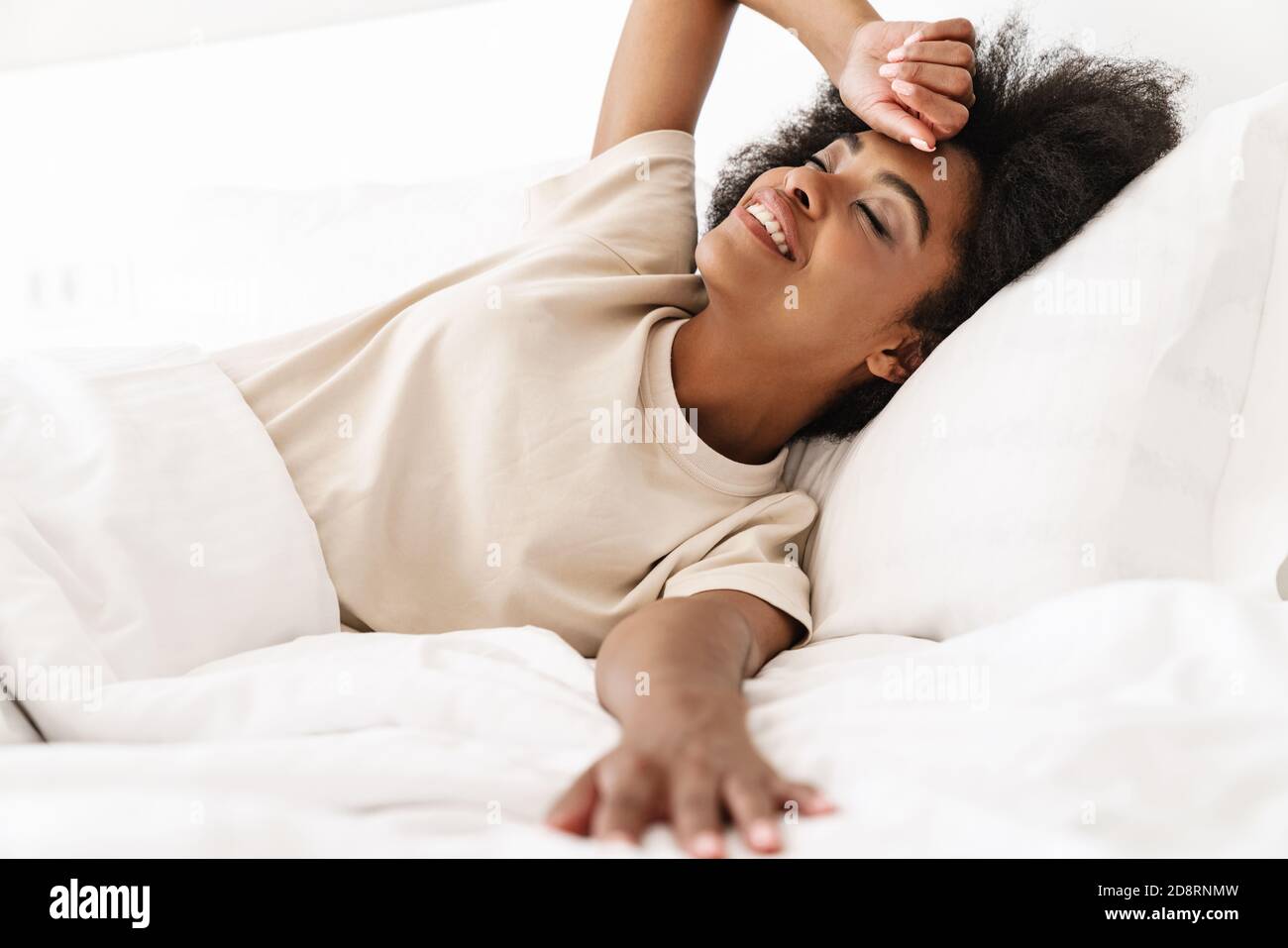 Beautiful young african woman lying in bed and stretching her arms ...