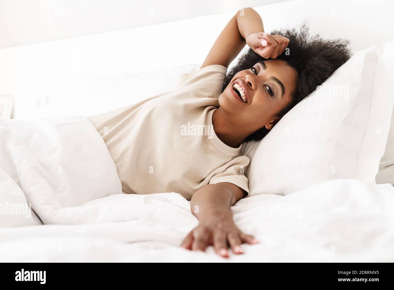 Beautiful young african woman lying in bed and stretching her arms ...