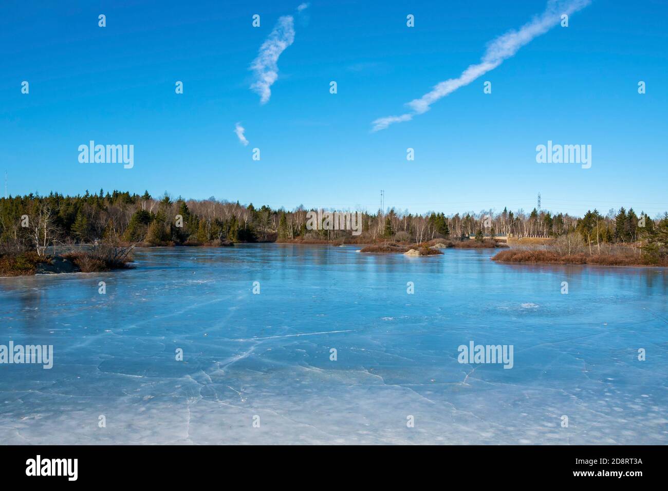 A frozen lake under a blue sky. The lake is blue ice with trees on the ...