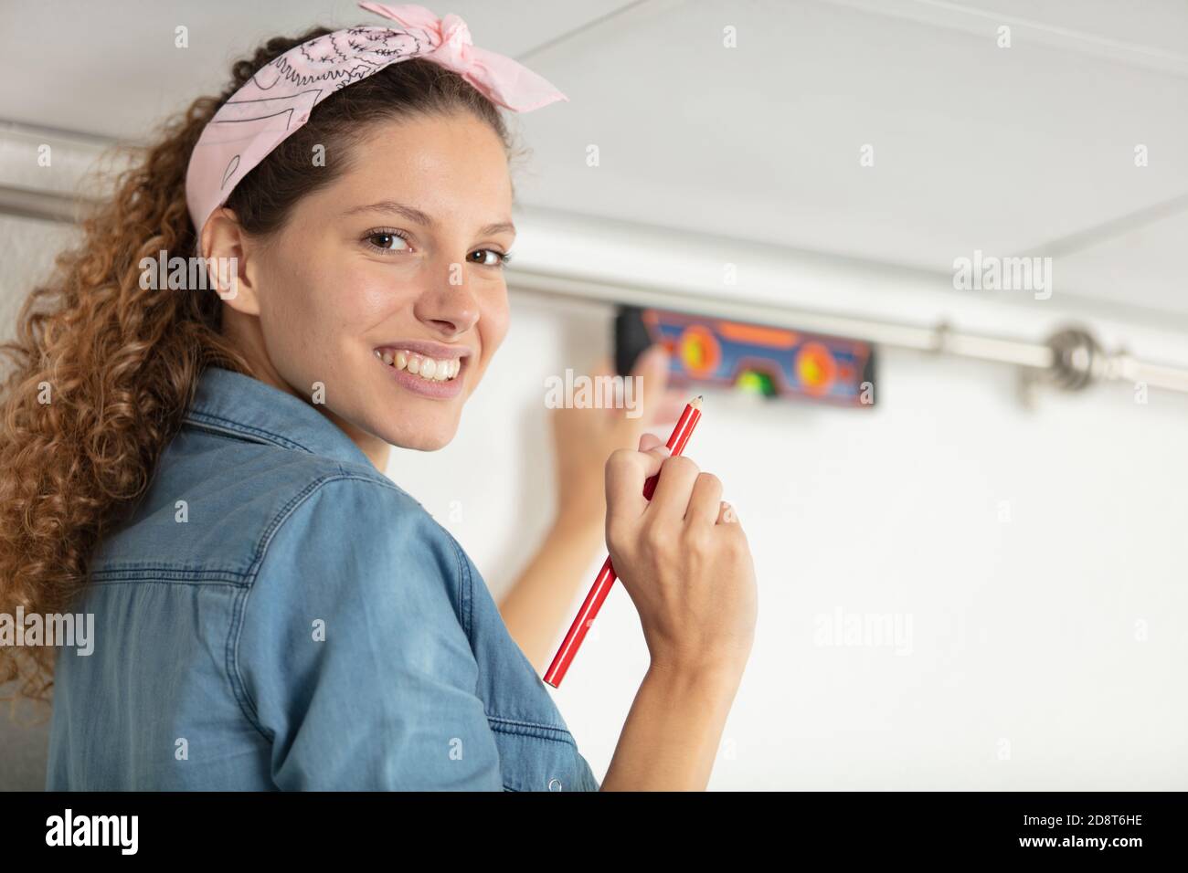 young woman using a spirit level and marking the wall Stock Photo - Alamy