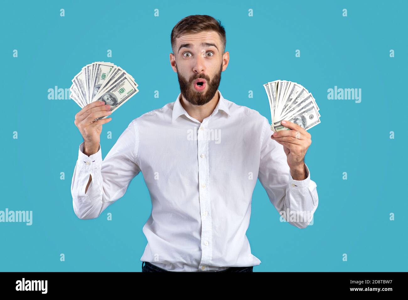 Shocked young man holding money banknotes on blue studio background ...