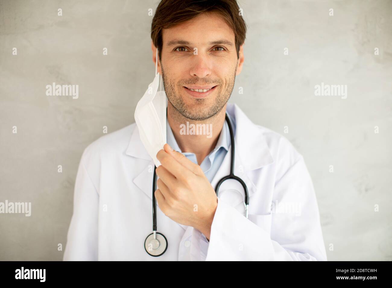 Attractive young male doctor taking off his surgical protective mask ...