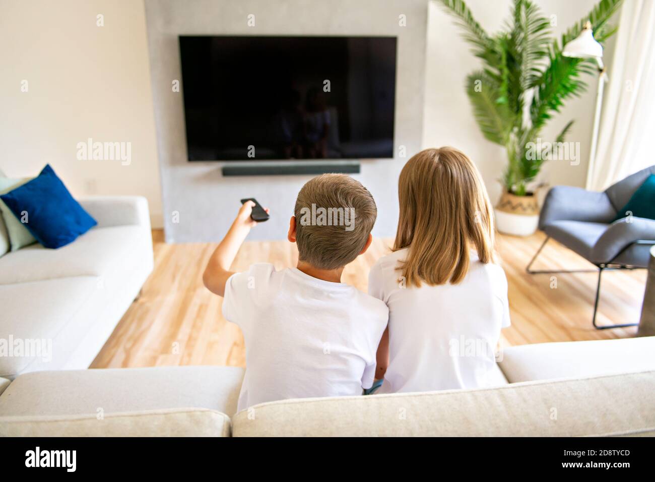 A two family brother and sister holding remote control and watching TV ...