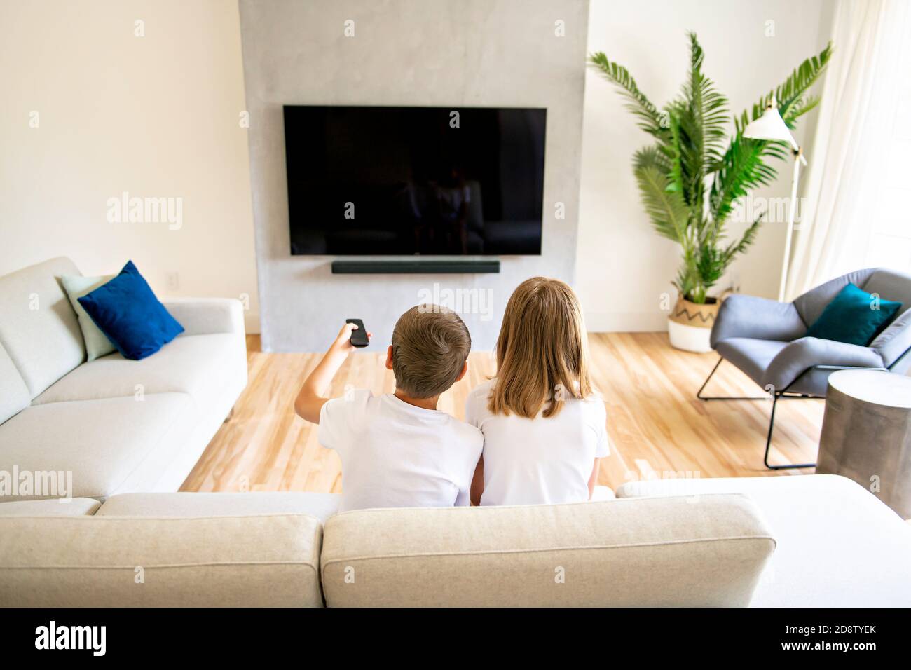 A two family brother and sister holding remote control and watching TV ...