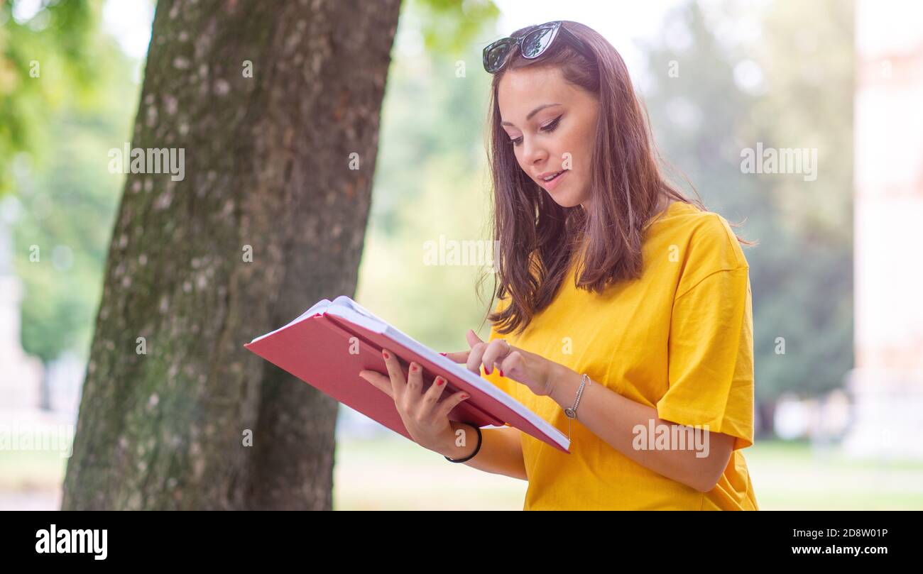 Portrait of a young girl reading a red book in a park in spring Stock ...