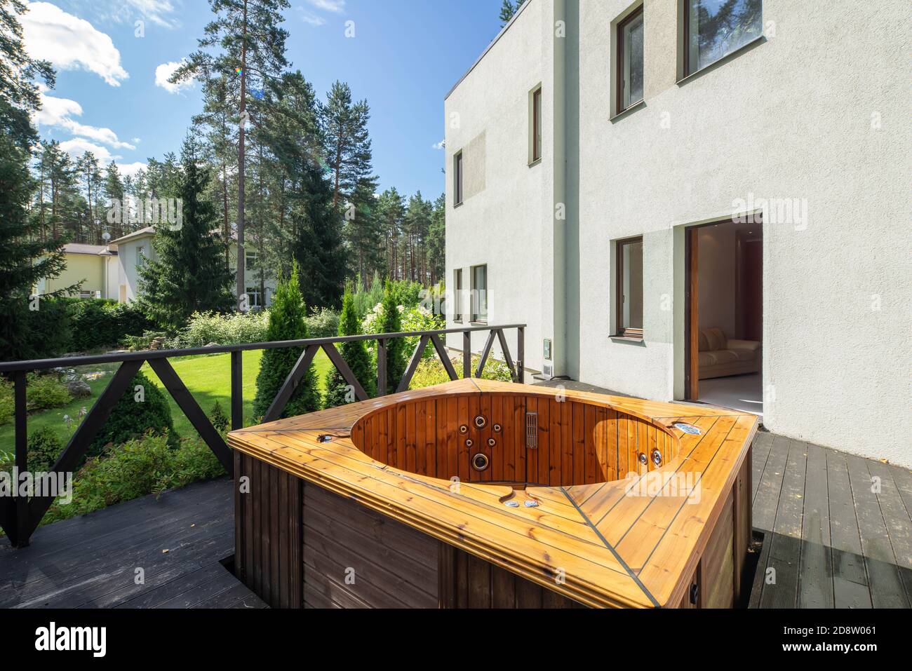 Outdoor wooden bath tub on terrace in private garden. Green trees and ...