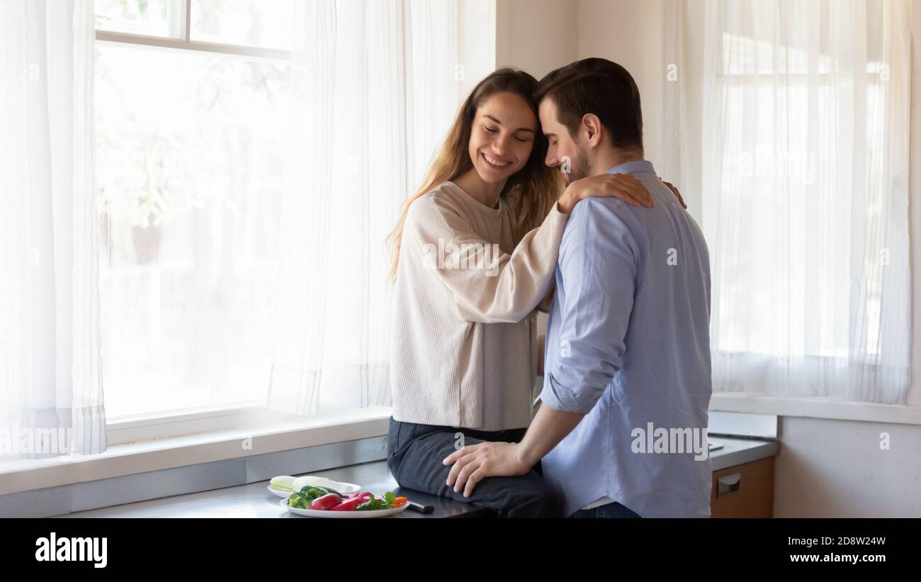 Young female sitting on kitchen countertop hugging male shoulders Stock ...