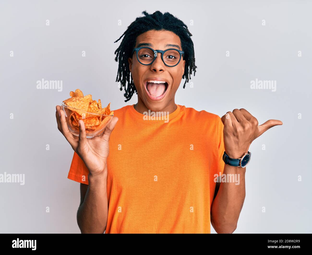 Young african american man holding nachos potato chips pointing thumb ...