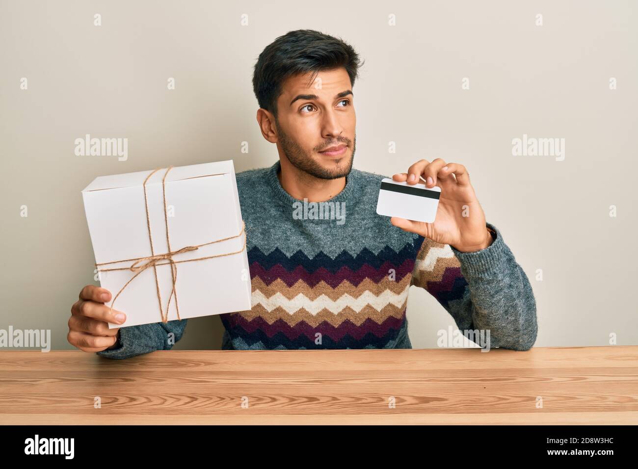 Young handsome man holding gift and credit card smiling looking to the ...