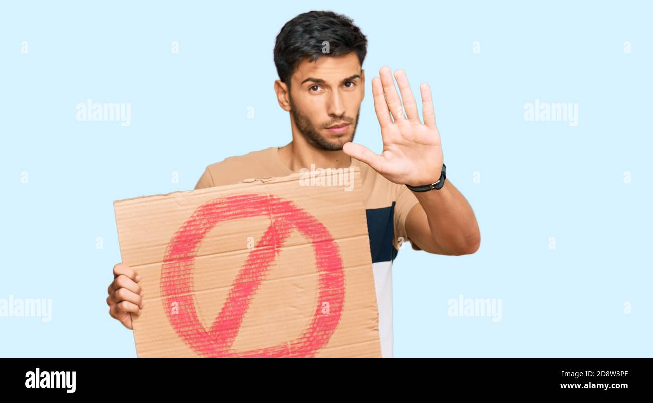 Young handsome man holding prohibited warning banner with open hand ...