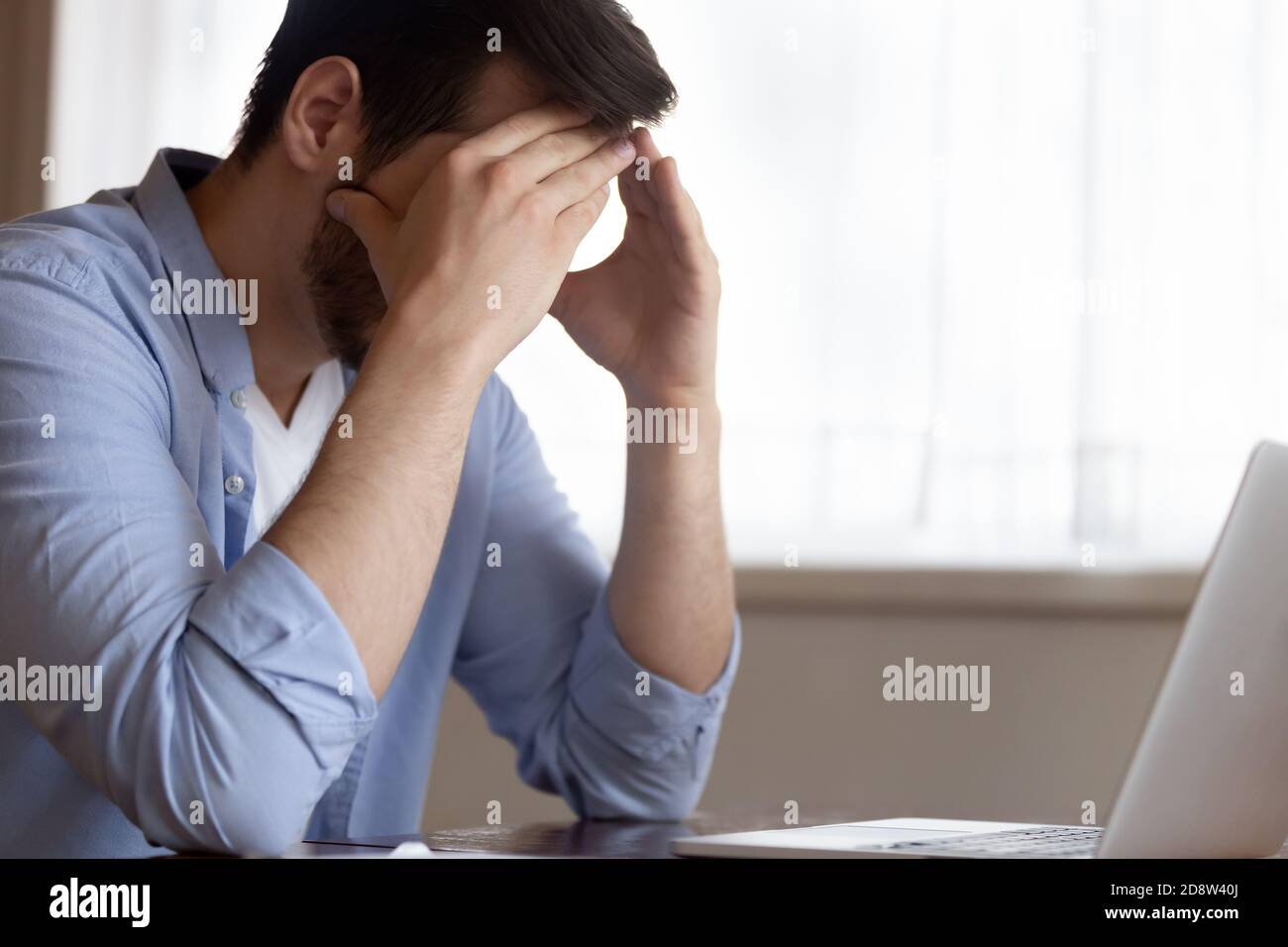 Exhausted young male employee sitting at workplace tired from work ...