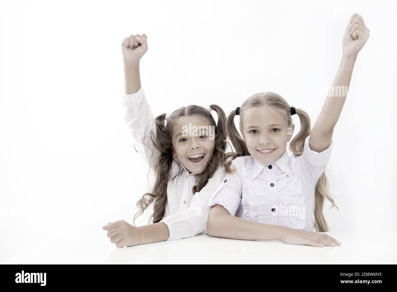 Schoolgirls happy keep hands up while sit at desk white background. Win ...