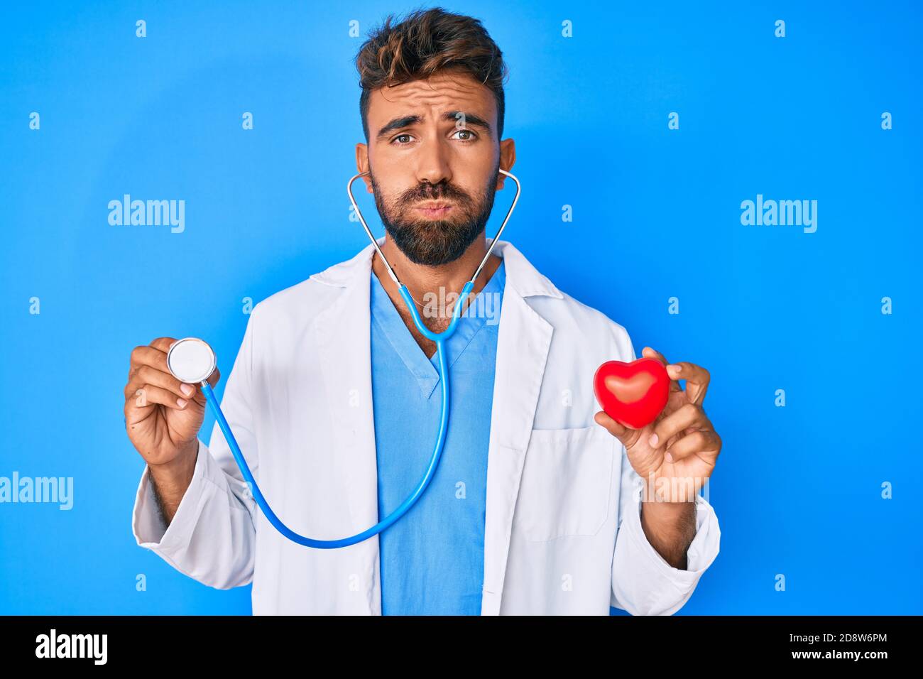 Young hispanic man wearing doctor uniform holding stethoscope and heart ...