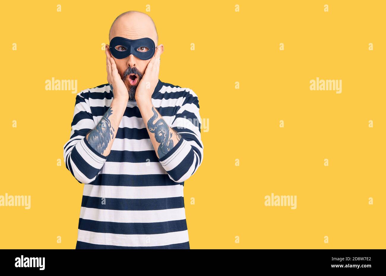 Young handsome man wearing burglar mask afraid and shocked, surprise ...
