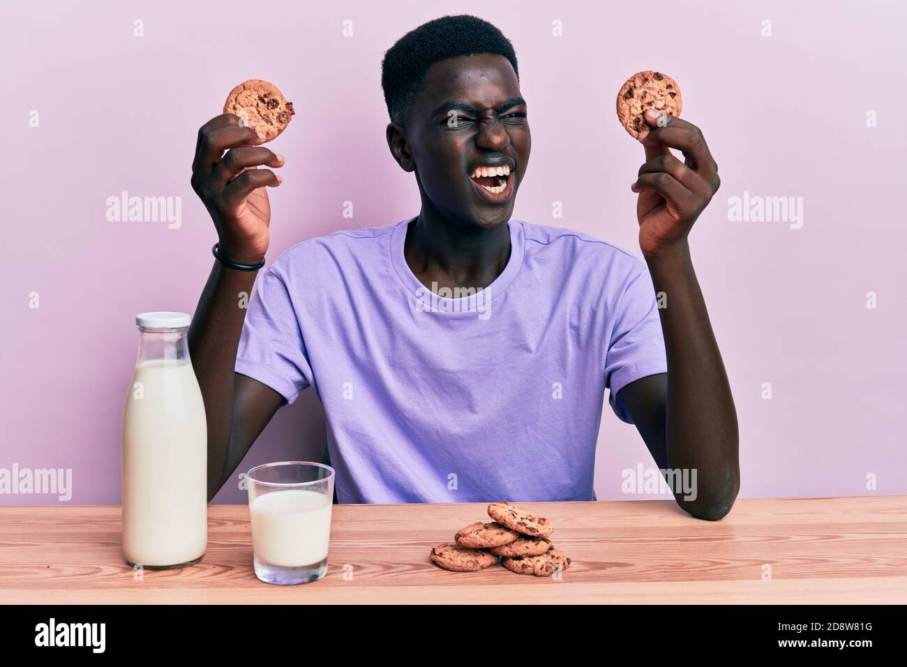 Young african american man drinking a glass of fresh milk with cookies ...