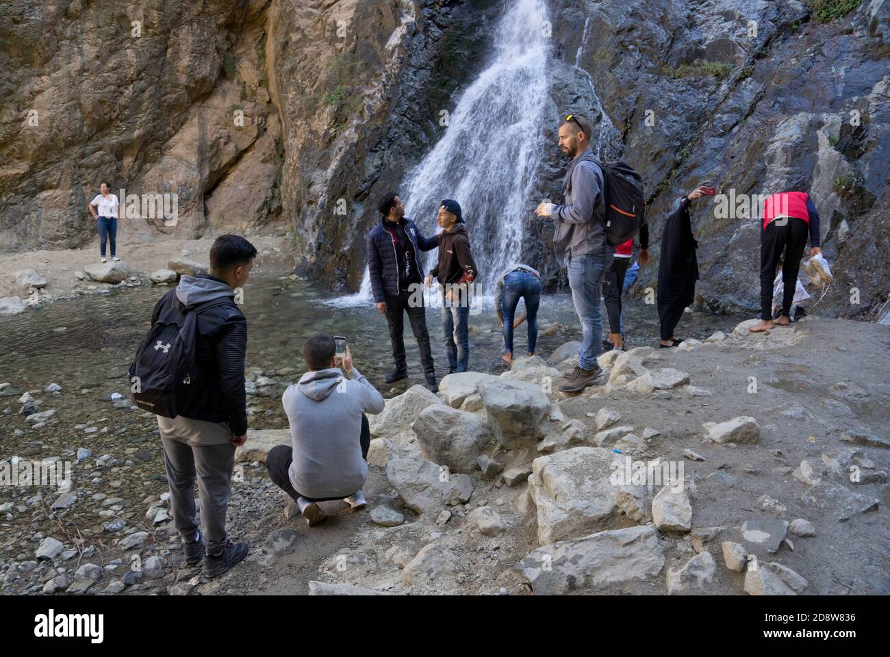 Tourists trekking by a waterfall in the High Atlas mountains in Morocco ...