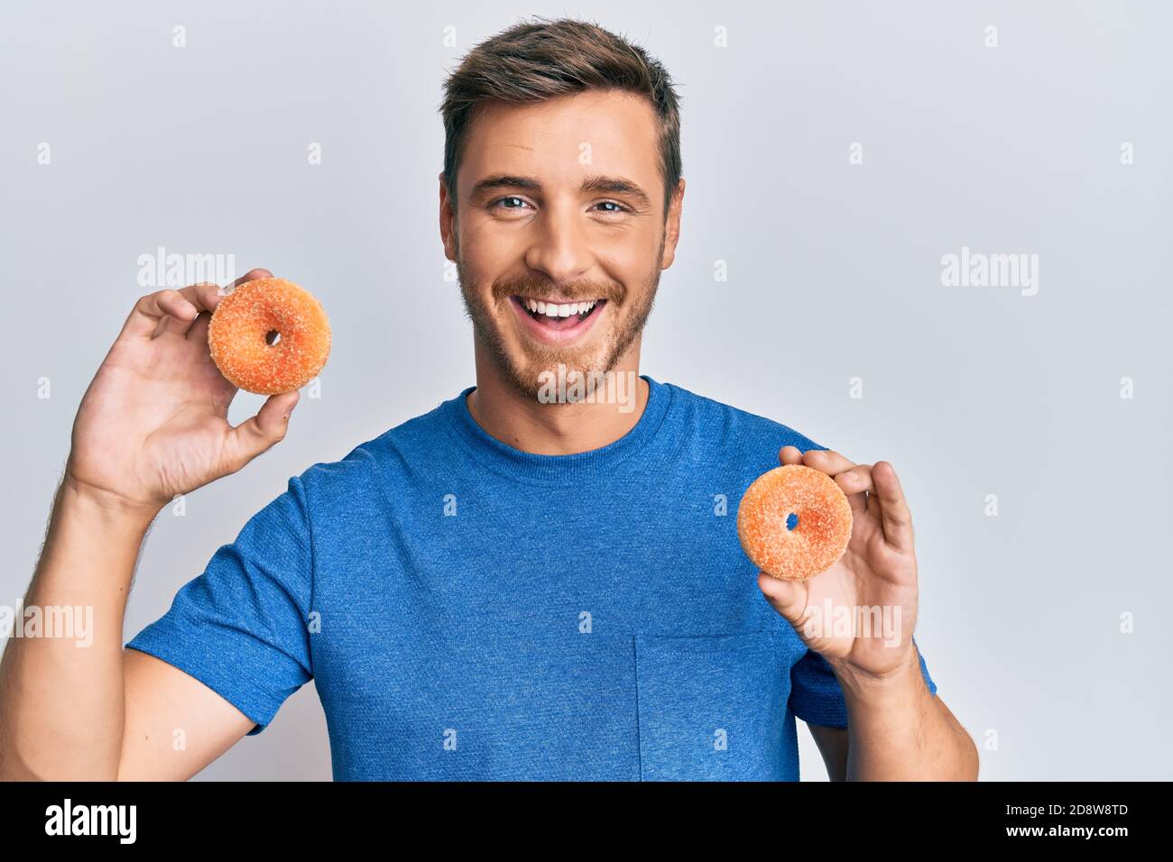 Handsome caucasian man eating donuts smiling and laughing hard out loud ...