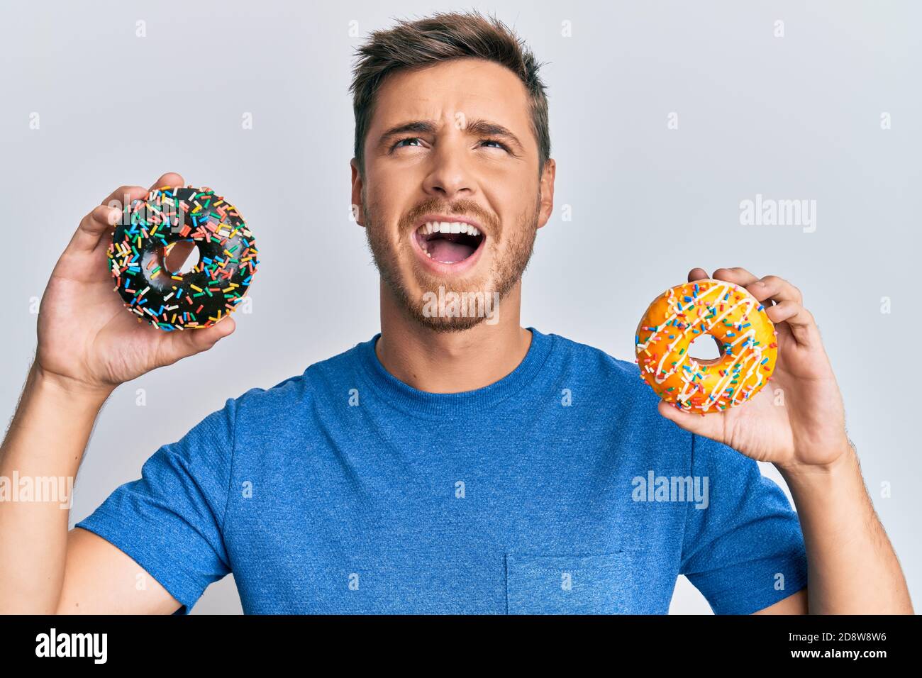 Handsome caucasian man holding tasty colorful doughnuts angry and mad ...