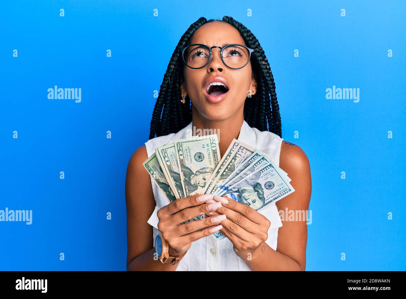 Beautiful hispanic woman holding dollars angry and mad screaming ...