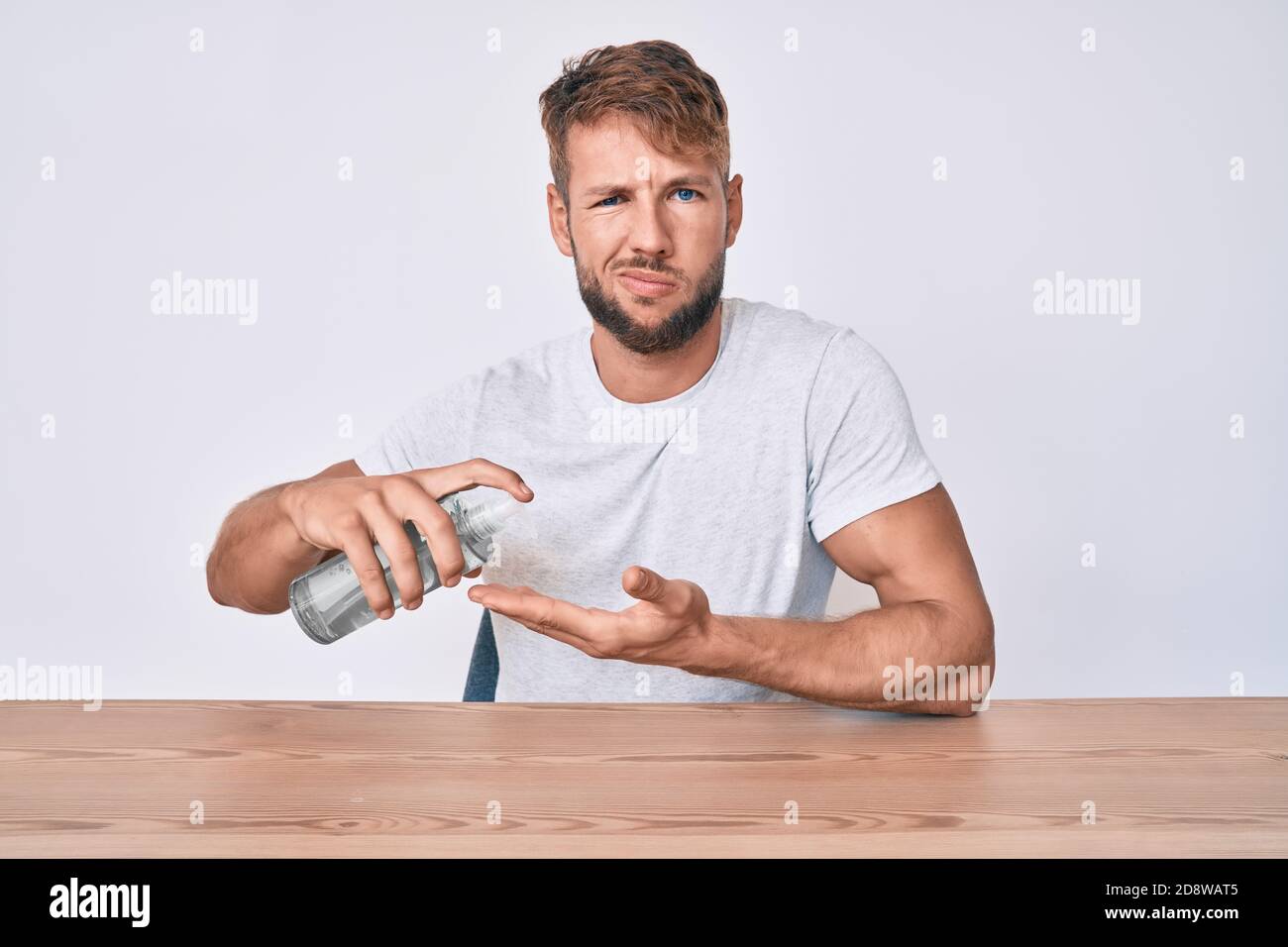 Young caucasian man using hand sanitizer gel sitting on the table ...