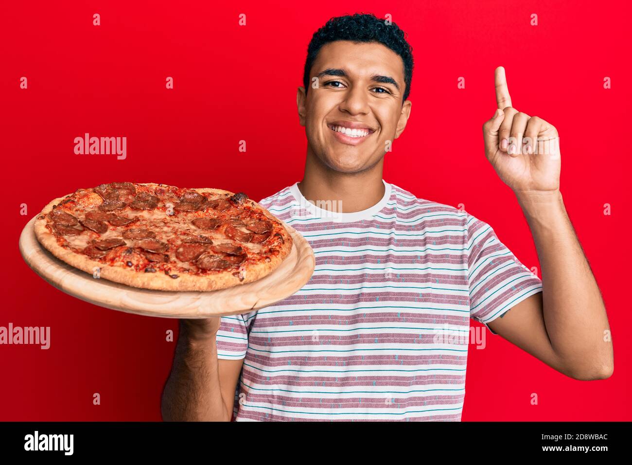 Young arab man holding italian pizza surprised with an idea or question ...