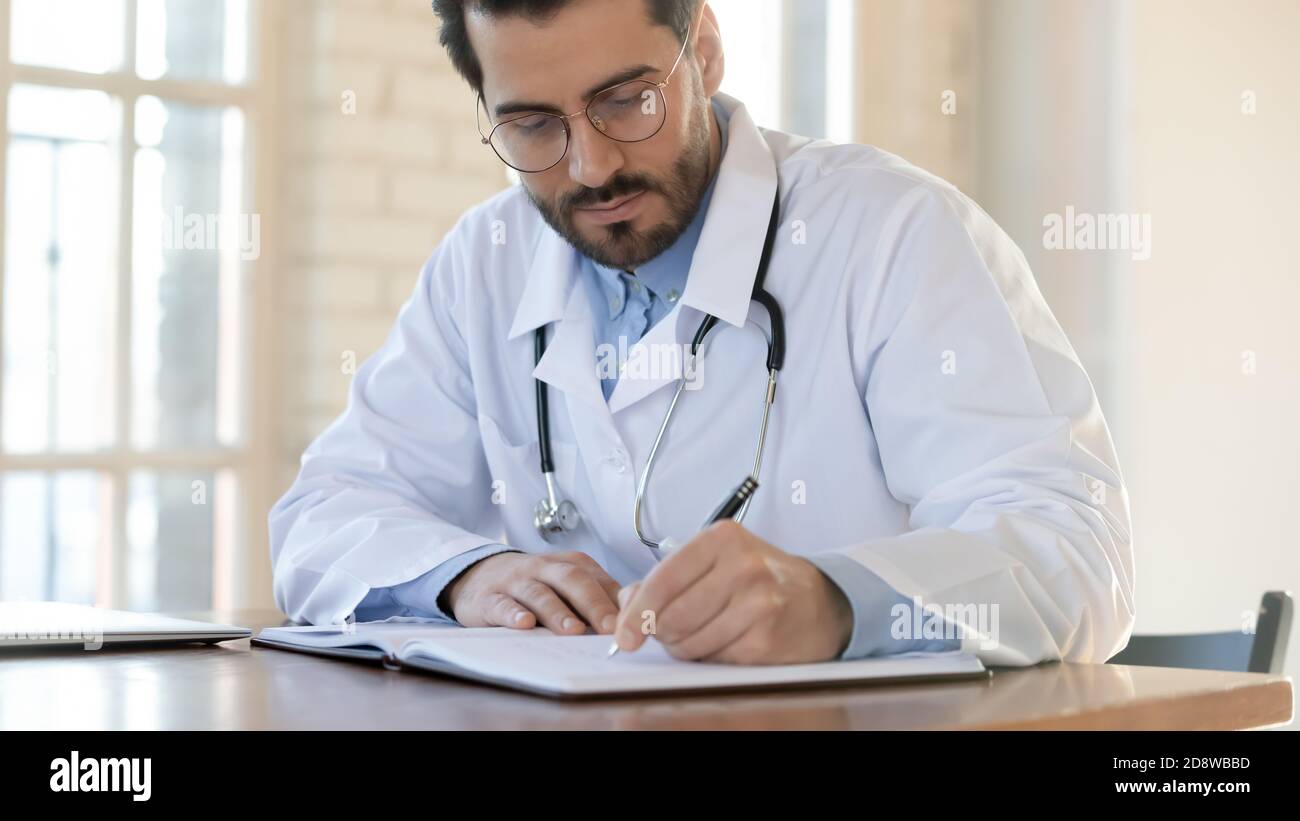 Serious attentive young male doctor focused on filling patient chart ...