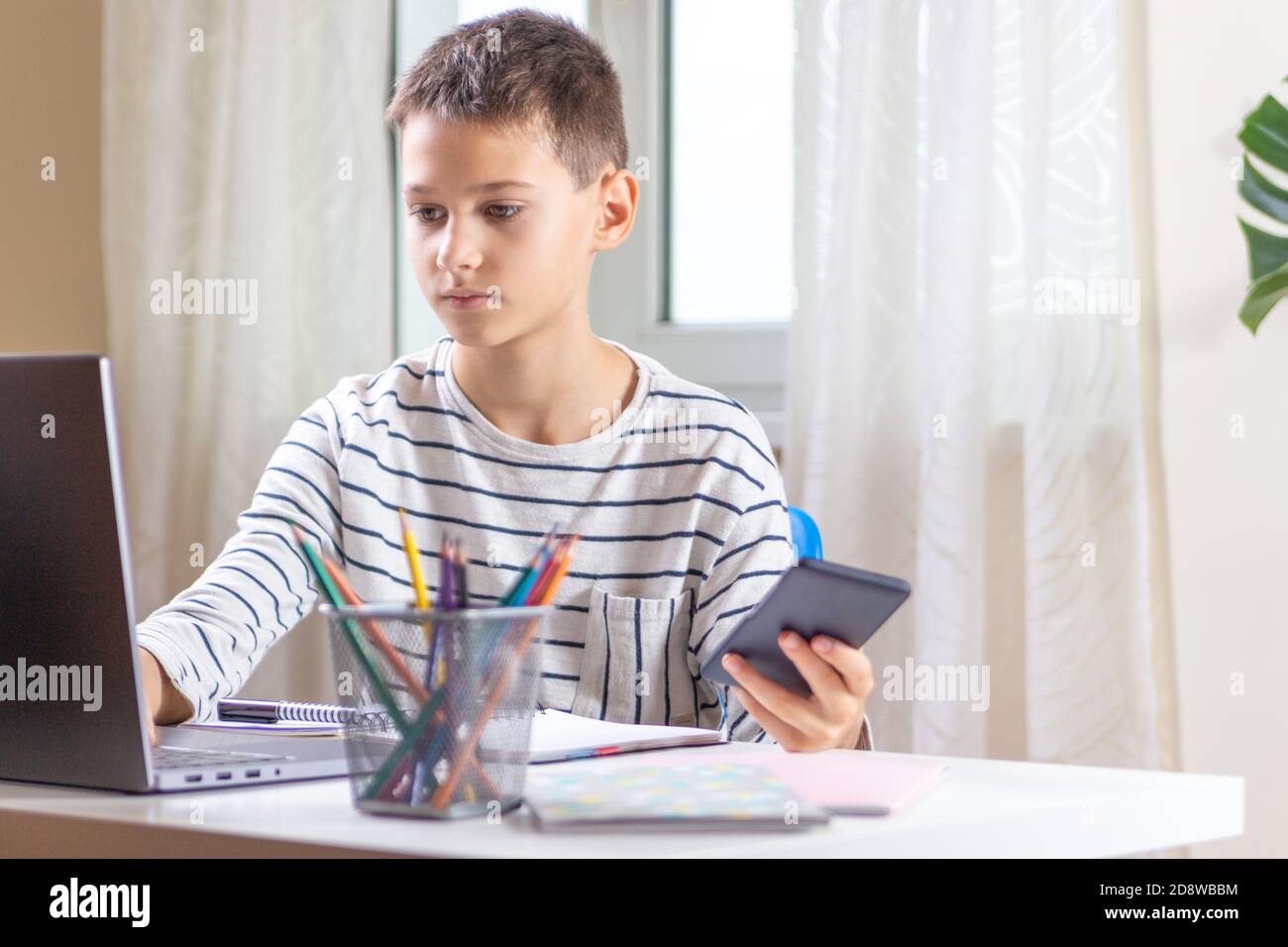 Kid sitting with laptop computer and scrolling phone instead of doing ...