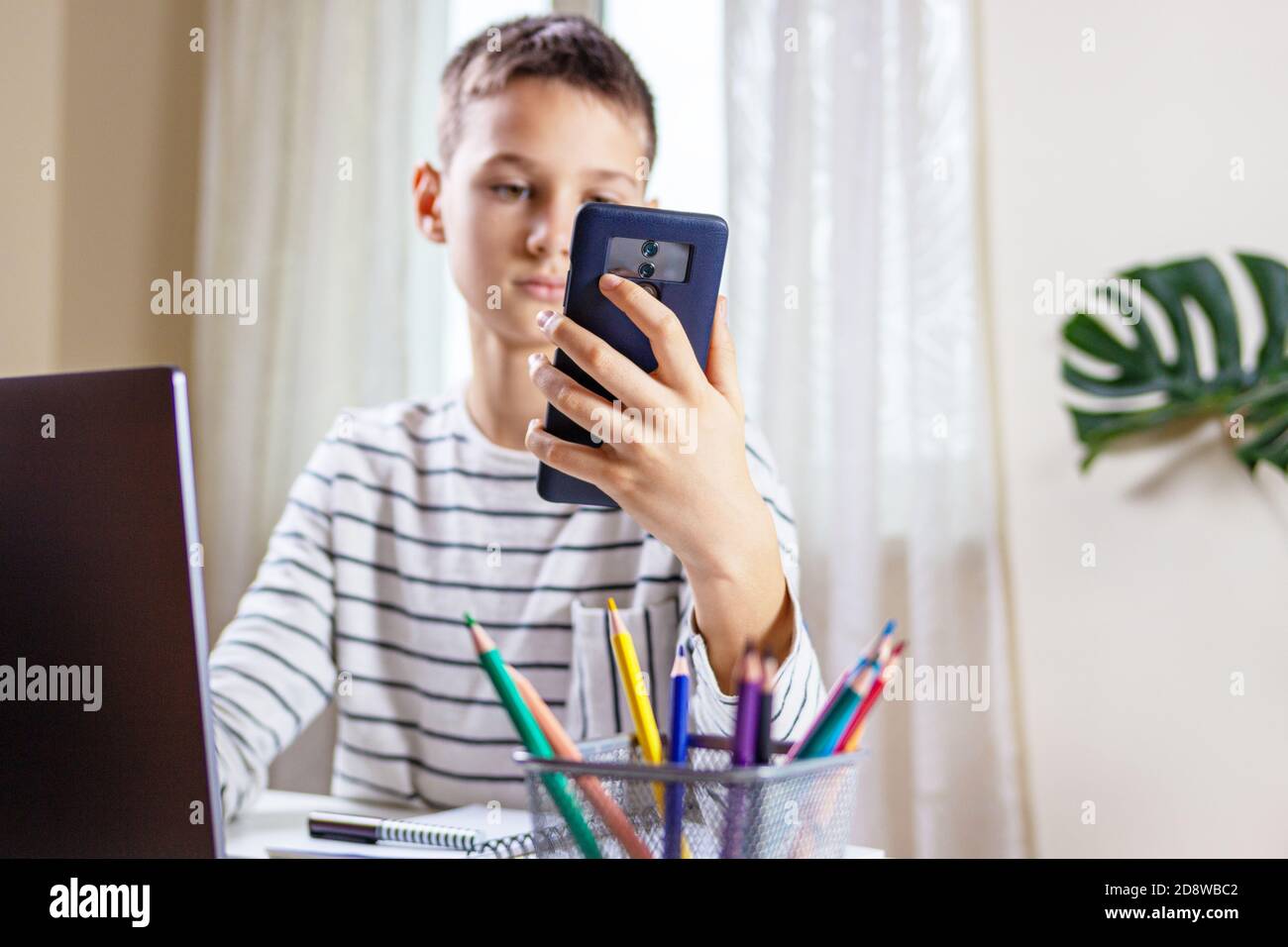 Kid sitting with laptop computer and scrolling phone instead of doing ...