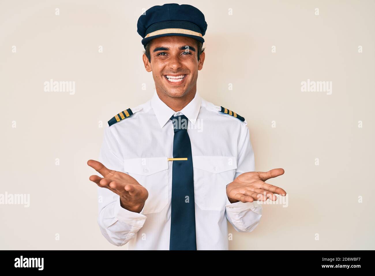 Young hispanic man wearing airplane pilot uniform smiling cheerful with ...