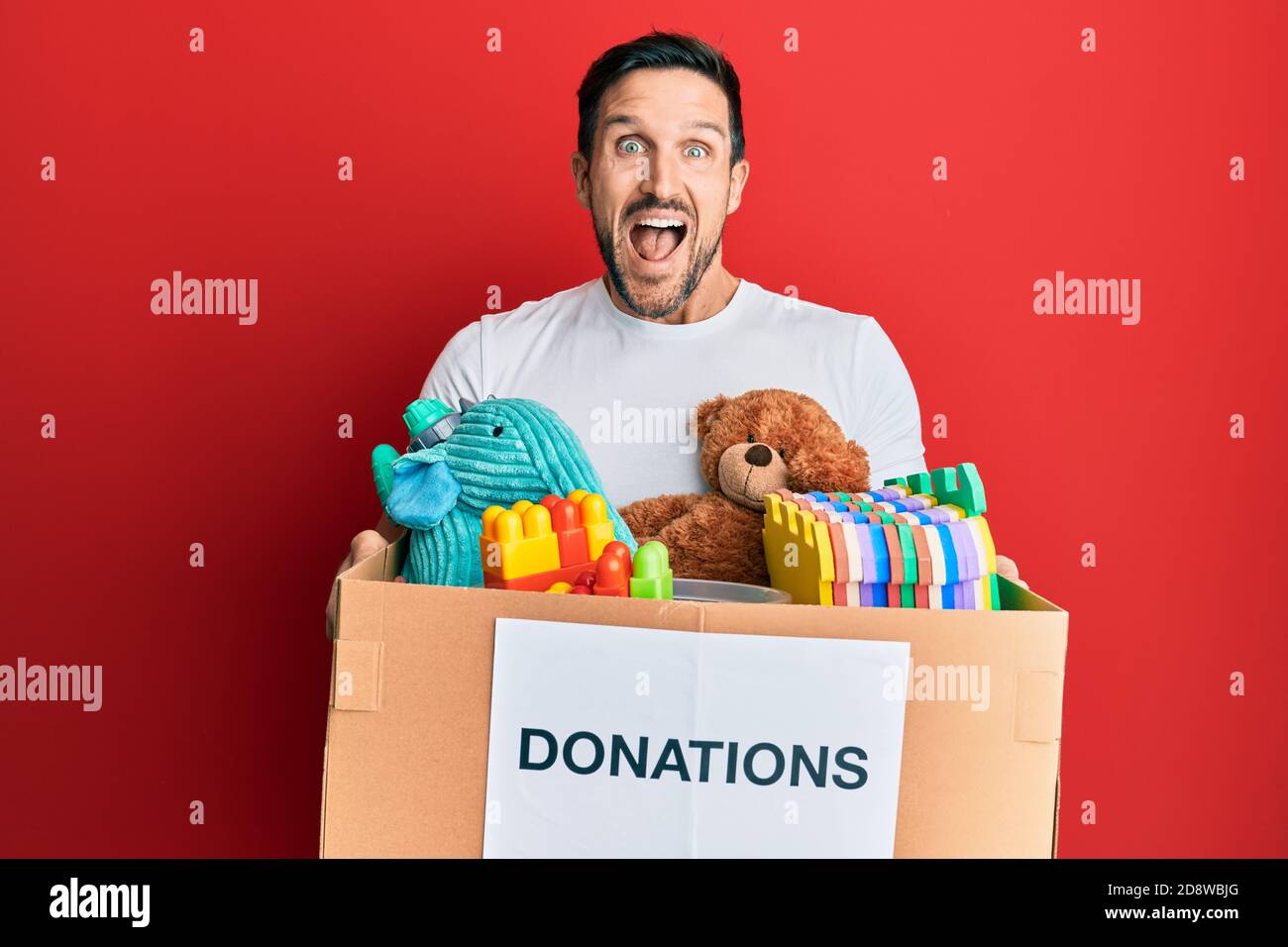 Young handsome man holding donation box with toys celebrating crazy and ...