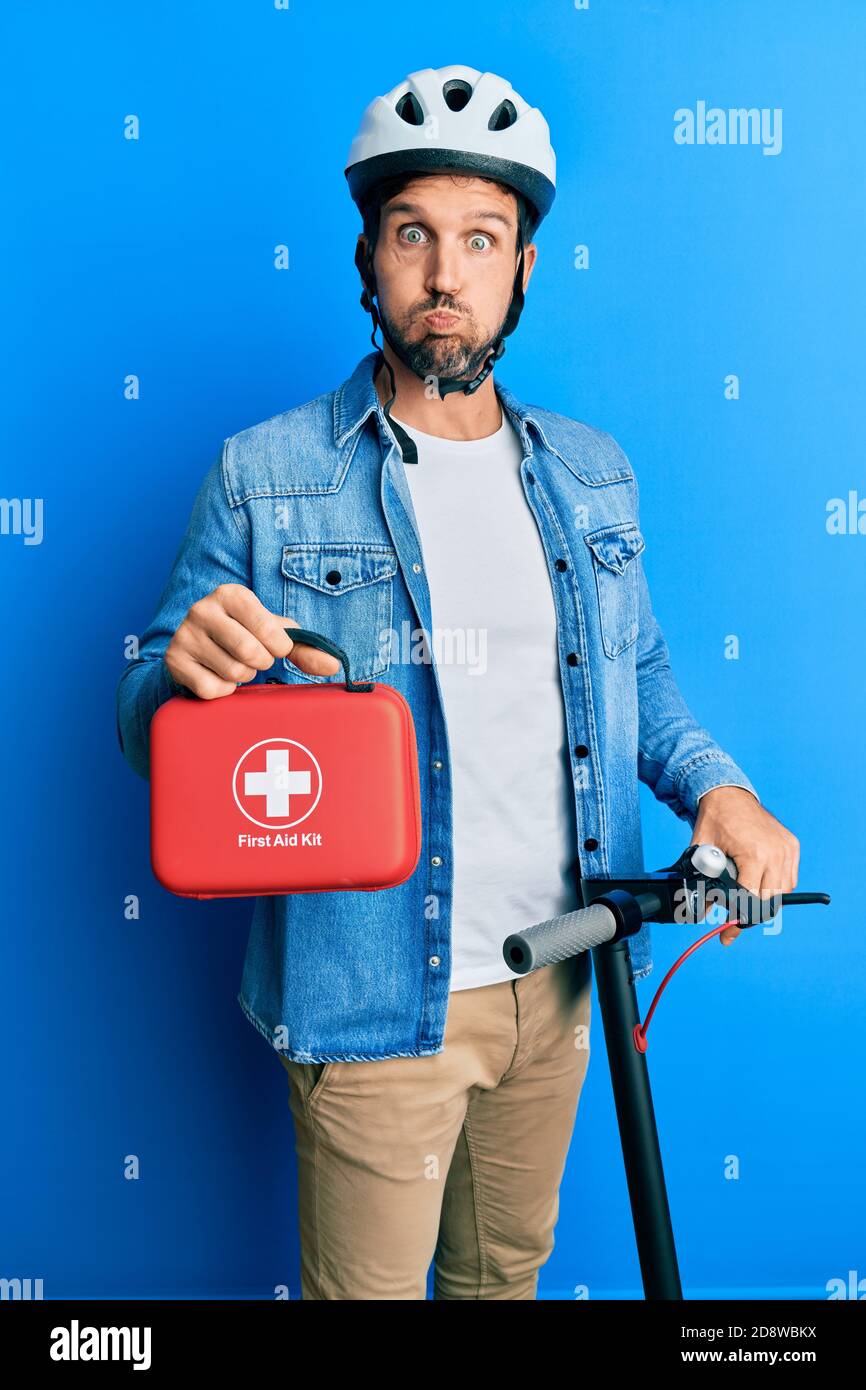Young man standing on scooter wearing helmet holding first aid kit ...