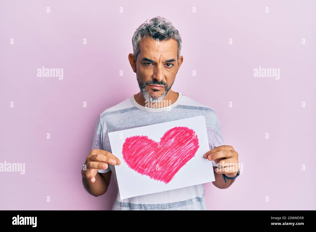 Middle age grey-haired man holding heart draw skeptic and nervous ...