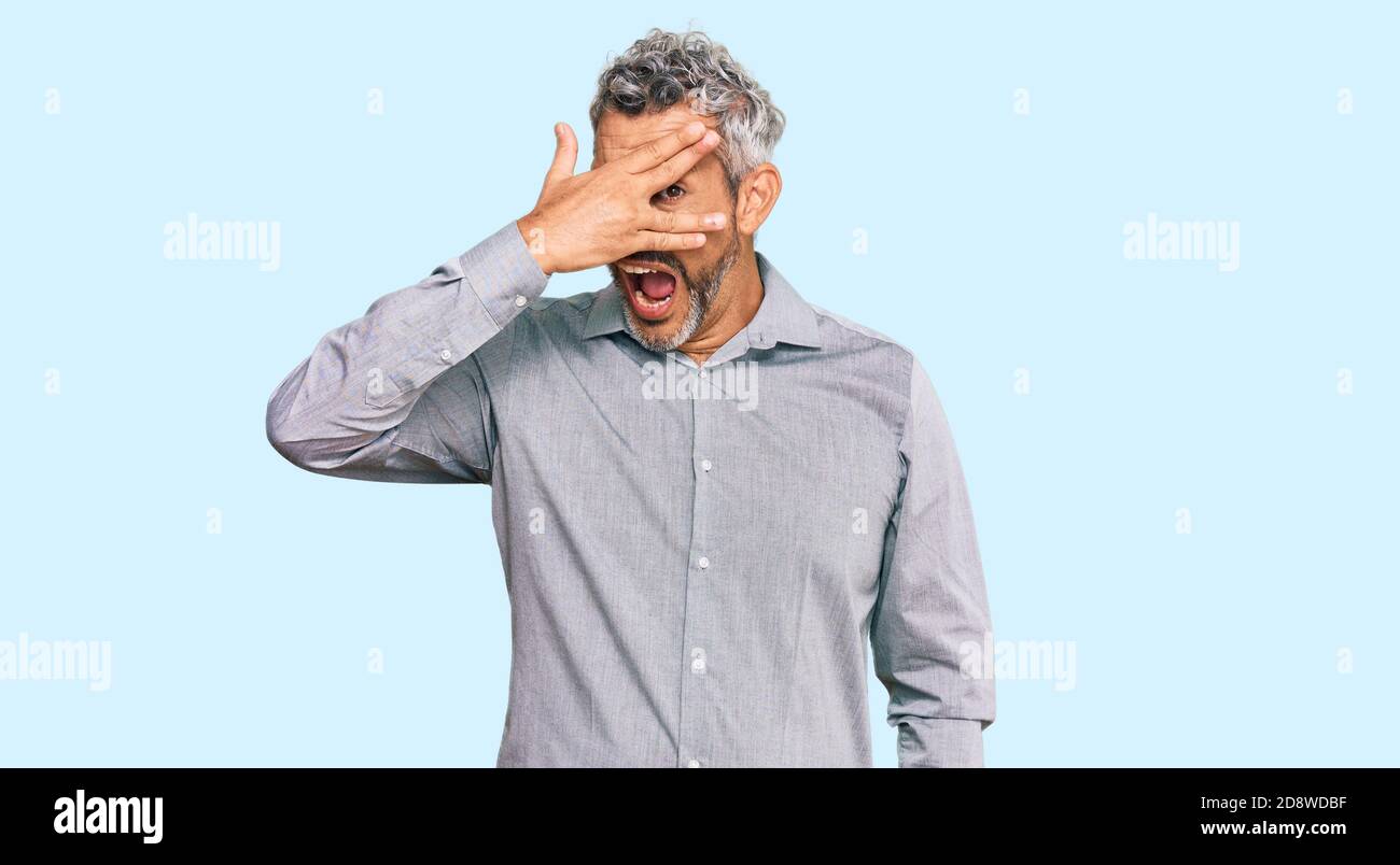 Middle age grey-haired man wearing casual clothes peeking in shock ...