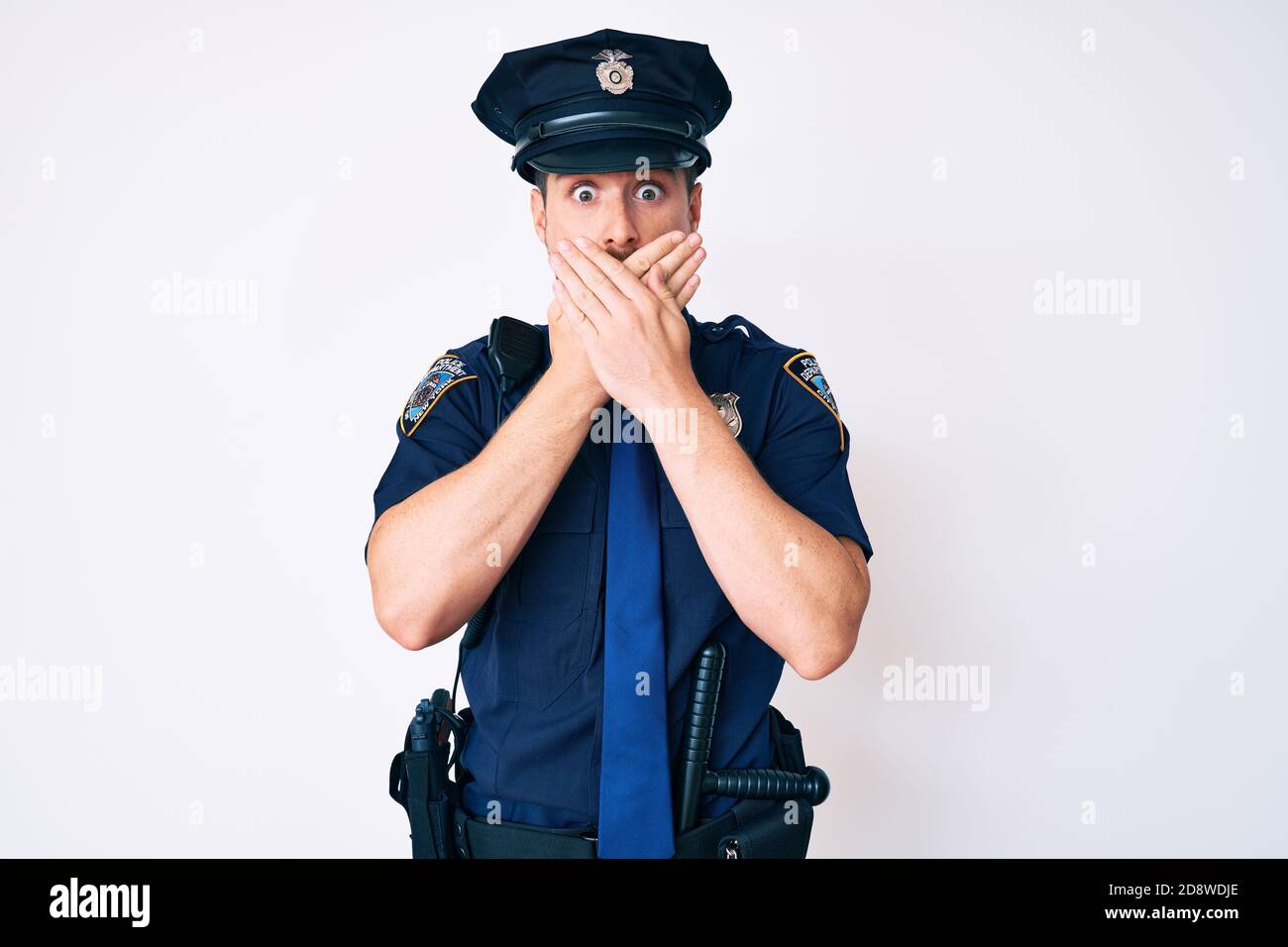 Young caucasian man wearing police uniform shocked covering mouth with ...